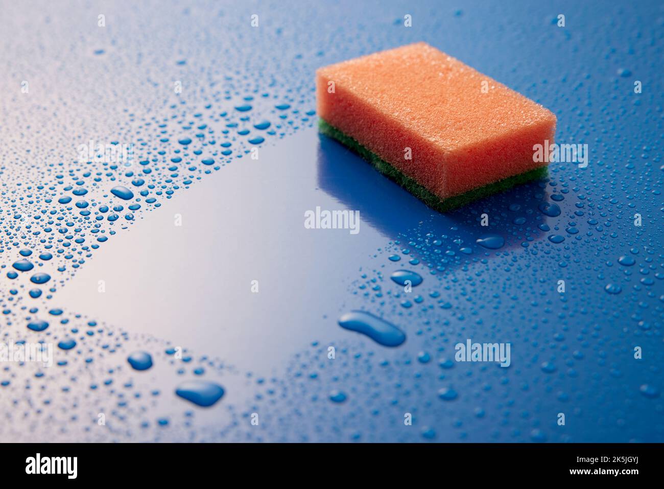 Orange scrub sponge placed on wet blue surface covered with small drops ...