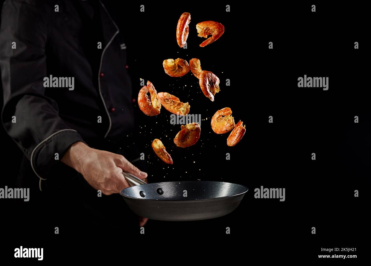 Crop anonymous male chef tossing prawns in frying pan while cooking ...