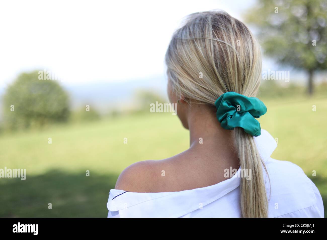 A young blonde woman from behind, wearing a white shirt and scrunchie ...