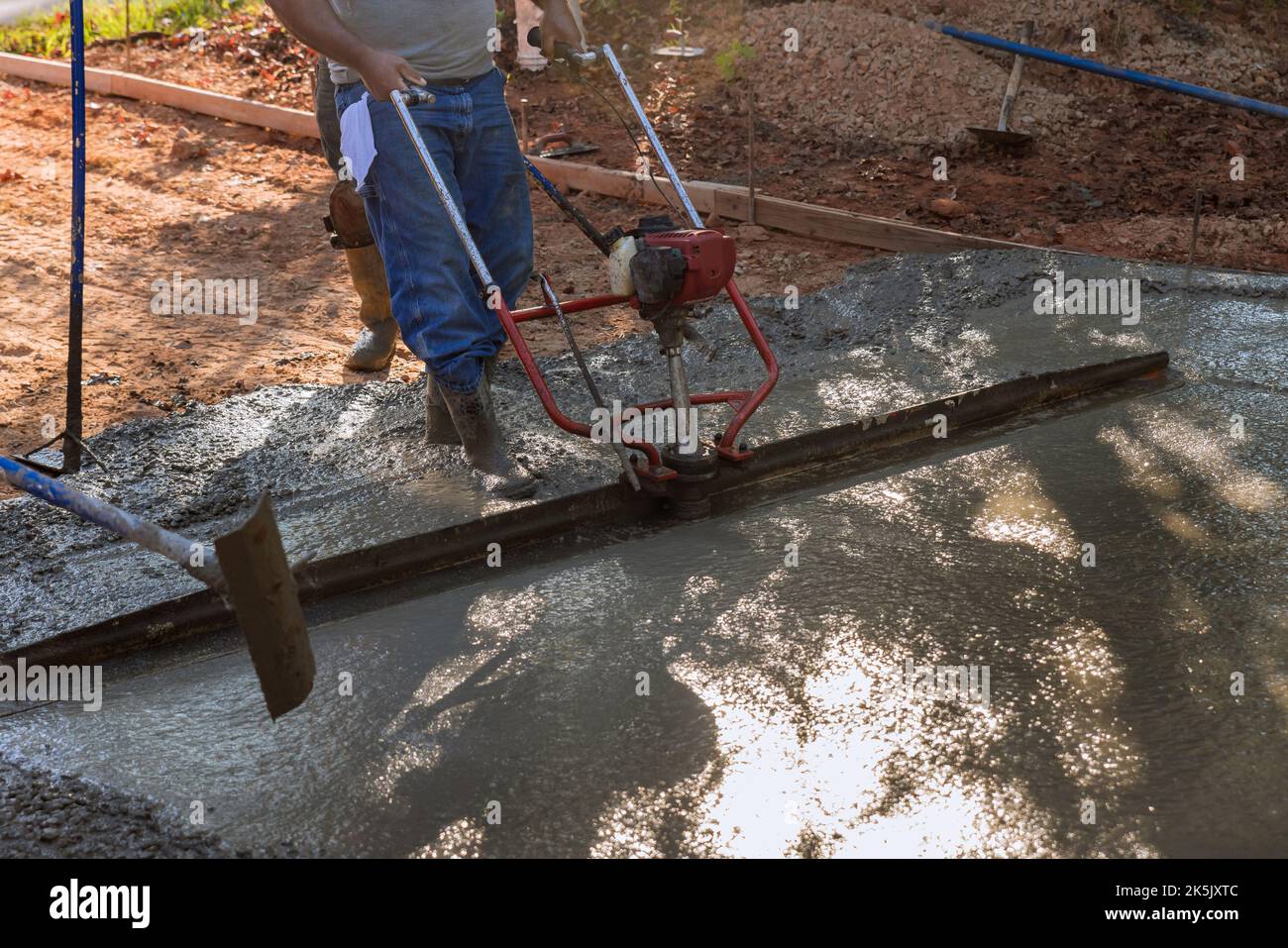 Machine is used to align compacted layer fresh concrete on new driveway ...
