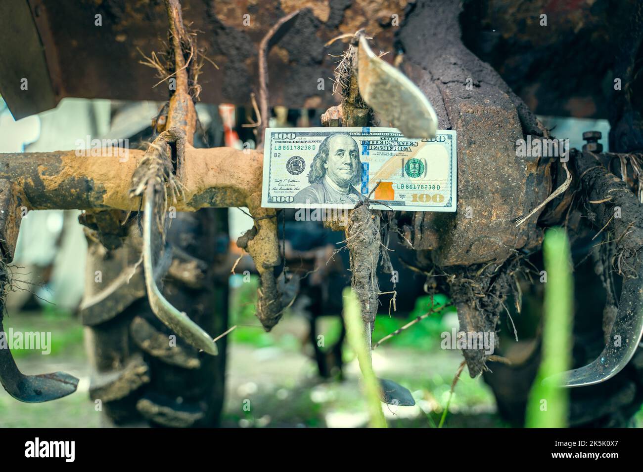 Hundred dollar bill between the teeth of a tractor rototiller close-up ...
