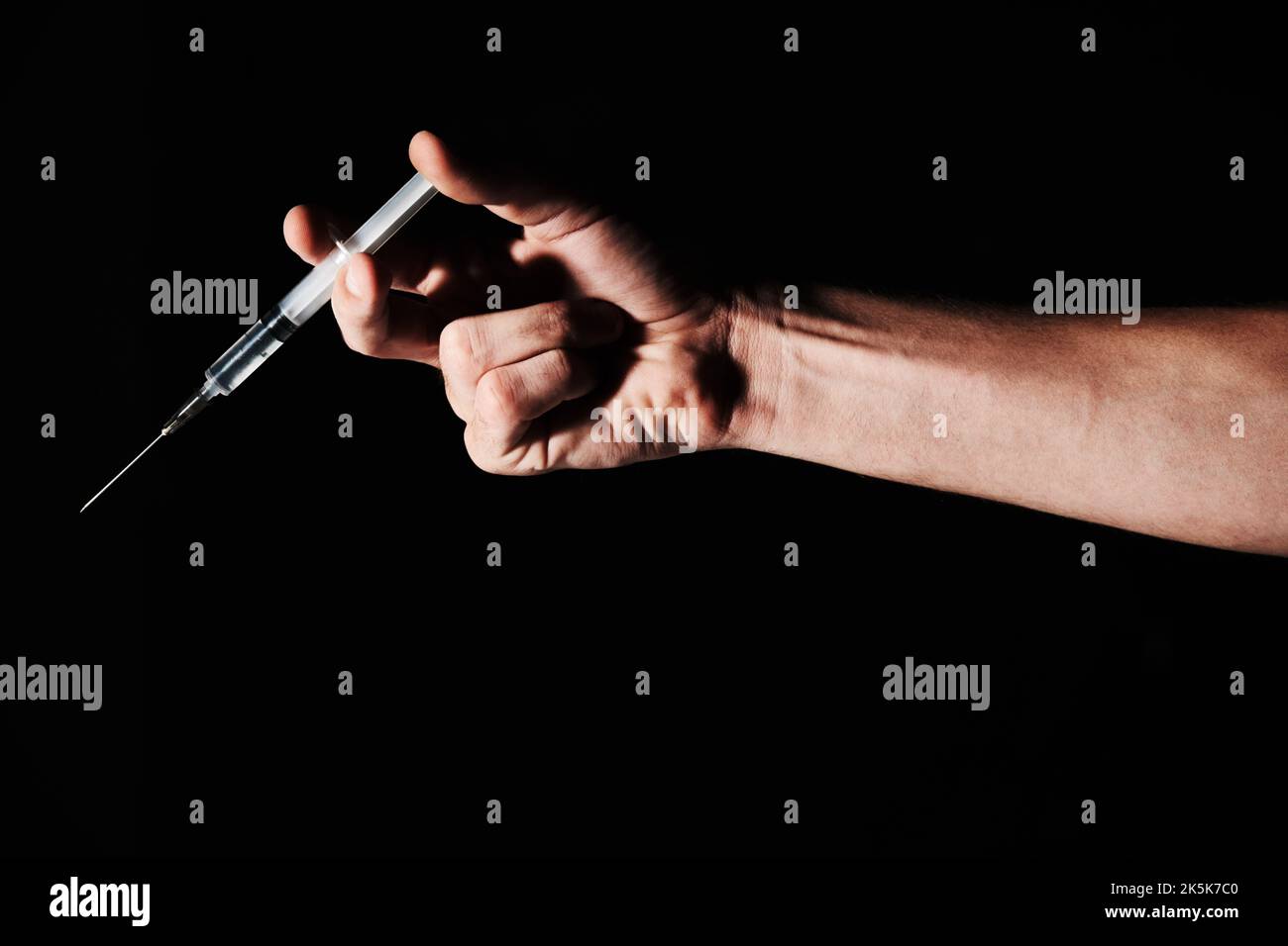 Getting an injection. A hand holding a syringe isolated against a black ...