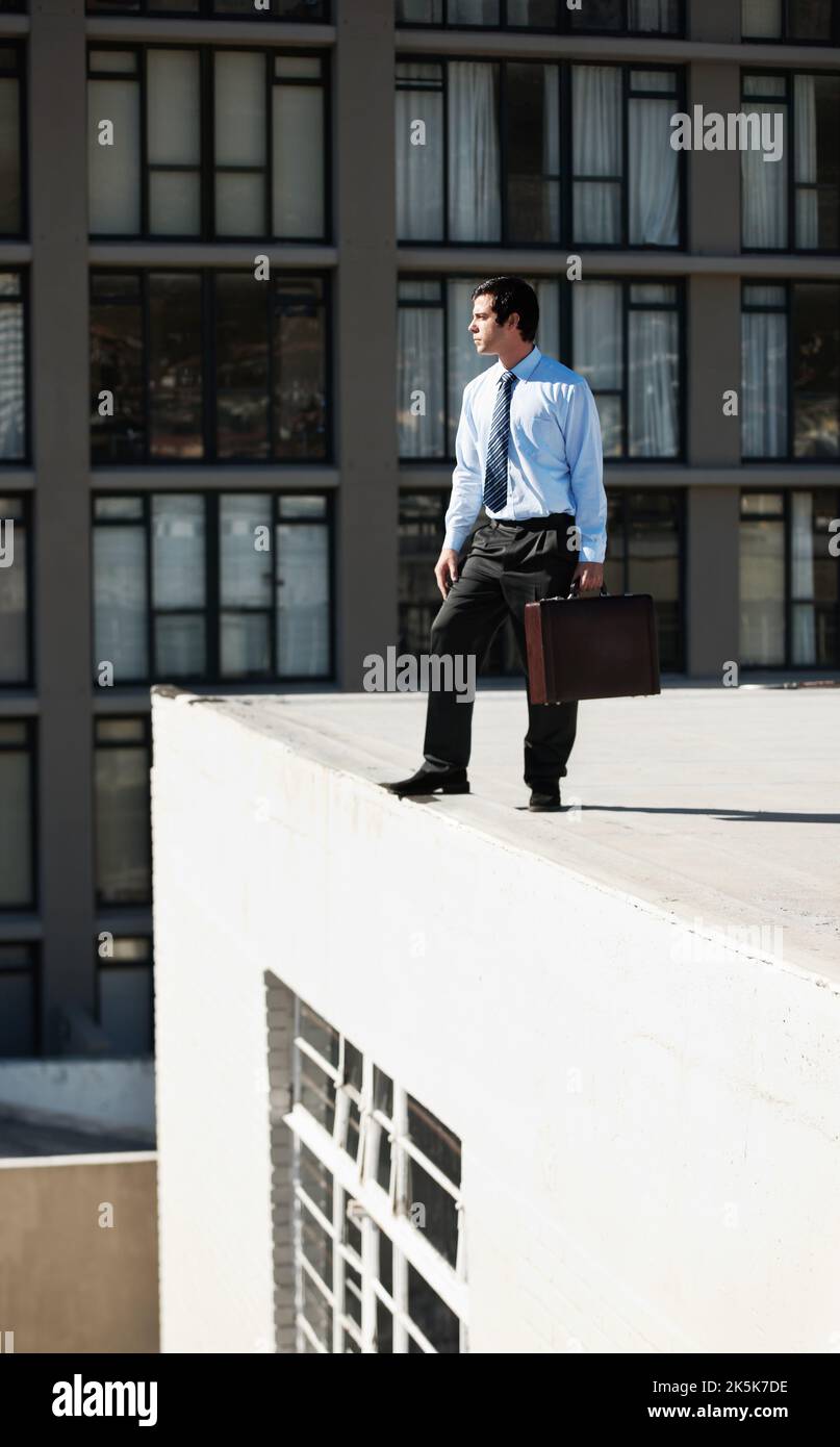 Living on the edge. A businessman standing on the edge of a building ...