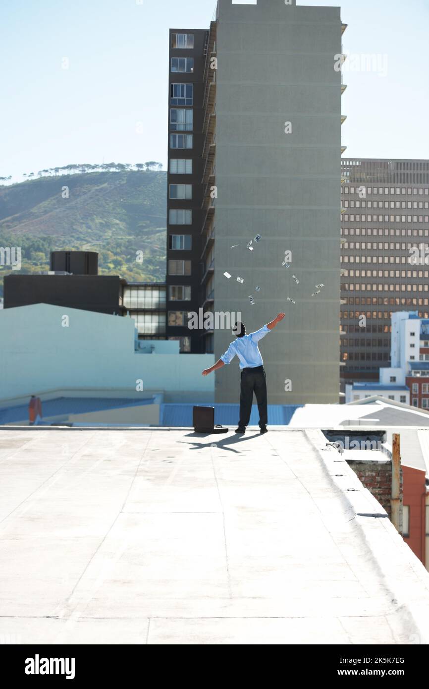 Freedom. A corporate man standing on the edge of a rooftop throwing ...