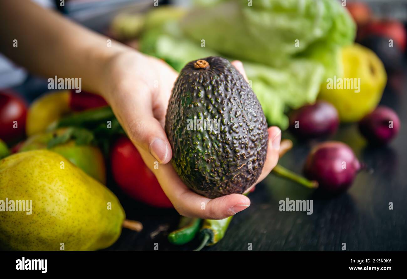 Avocado in a female hand on a blurred background with vegetables Stock ...