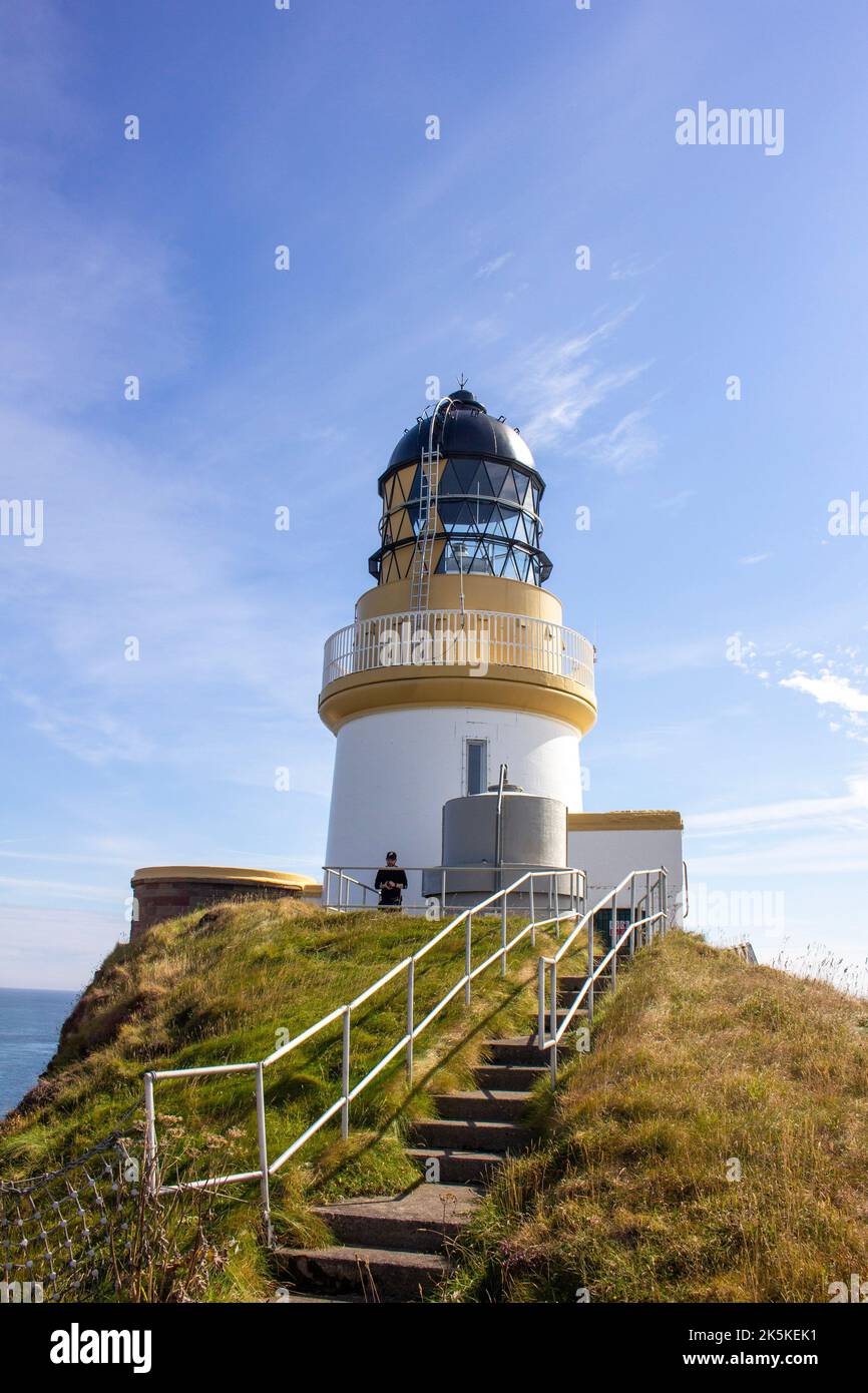 A vertical shot of a modern lighthouse on a hill under the blue clear ...