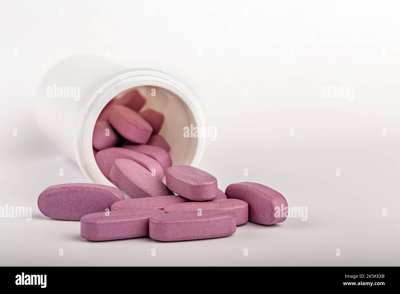 Pharmacology. Pink vitamins and tablets with container on white ...