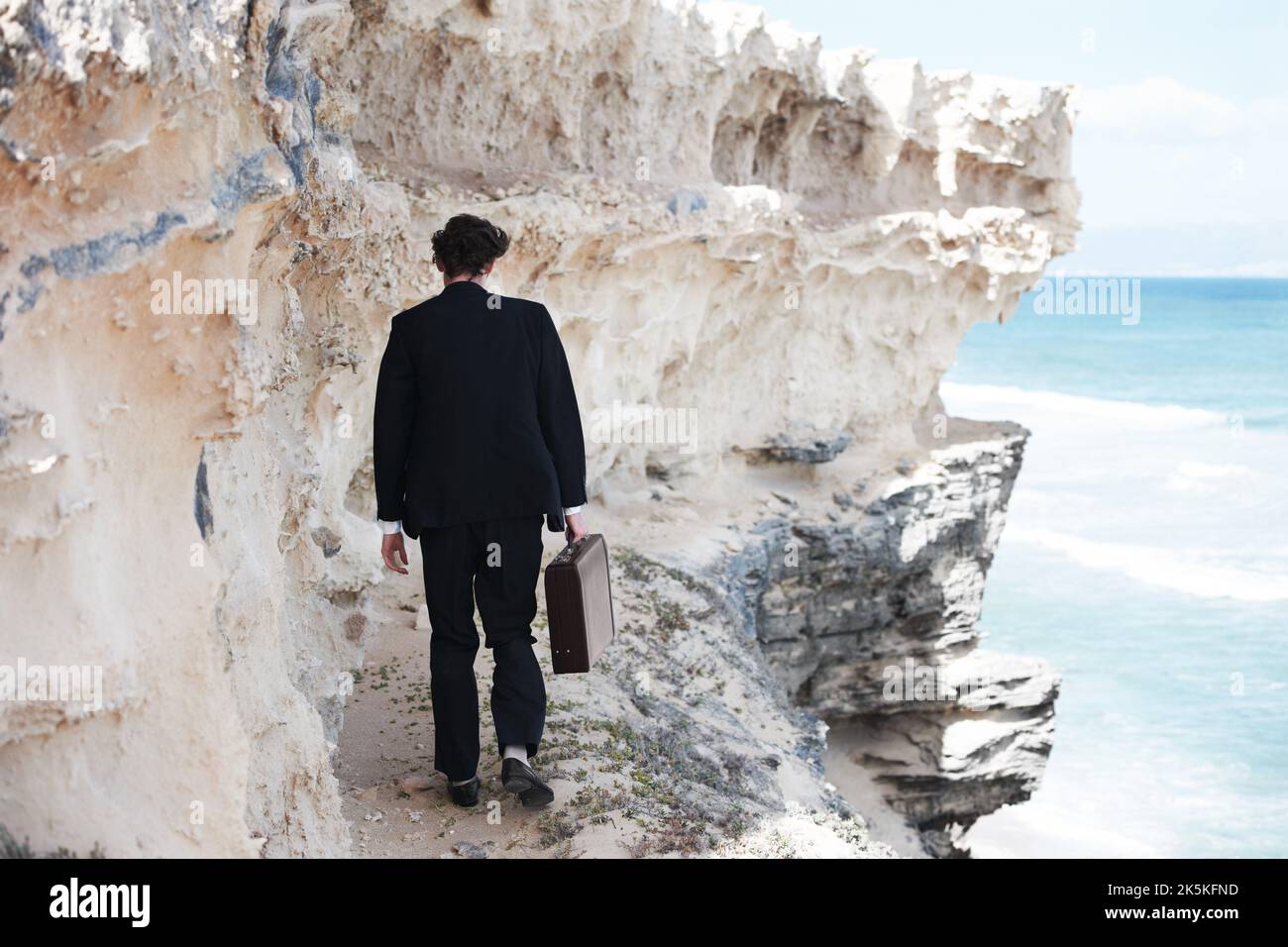 Taking the road less travelled. Businessman walking away on a ledge ...