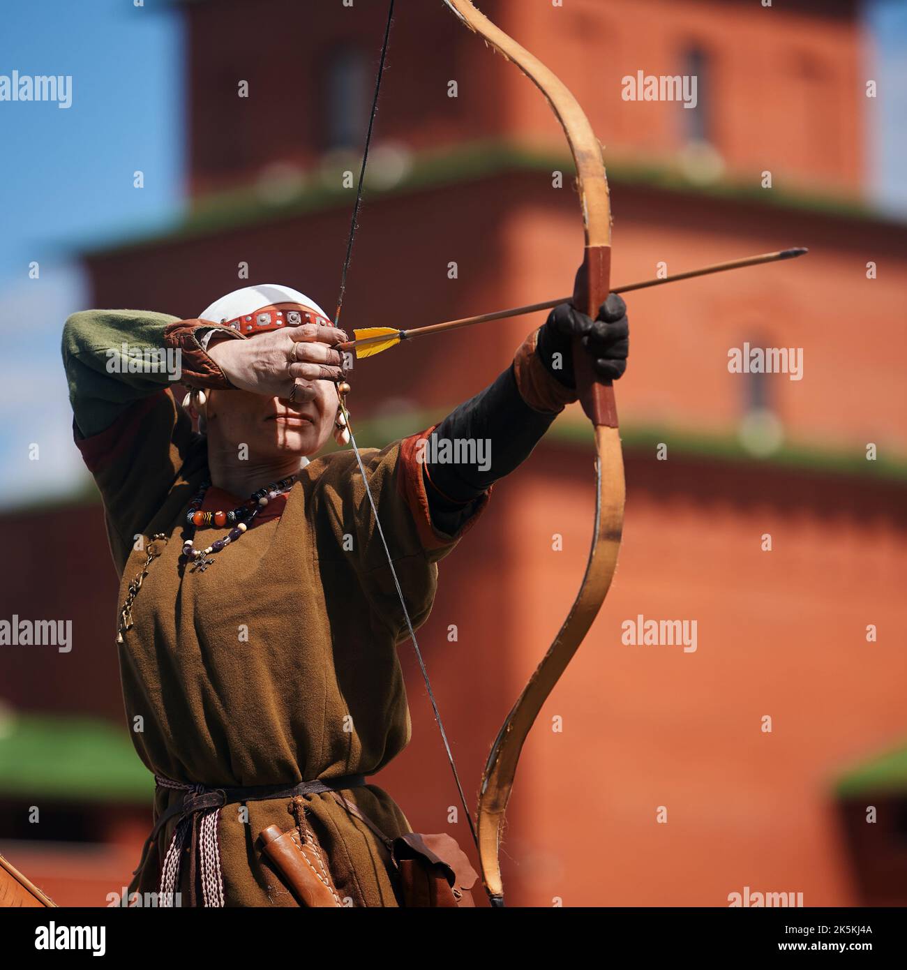 Medieval archery tournament. A woman shoots an arrow in the medieval castle yard. Woman in ...