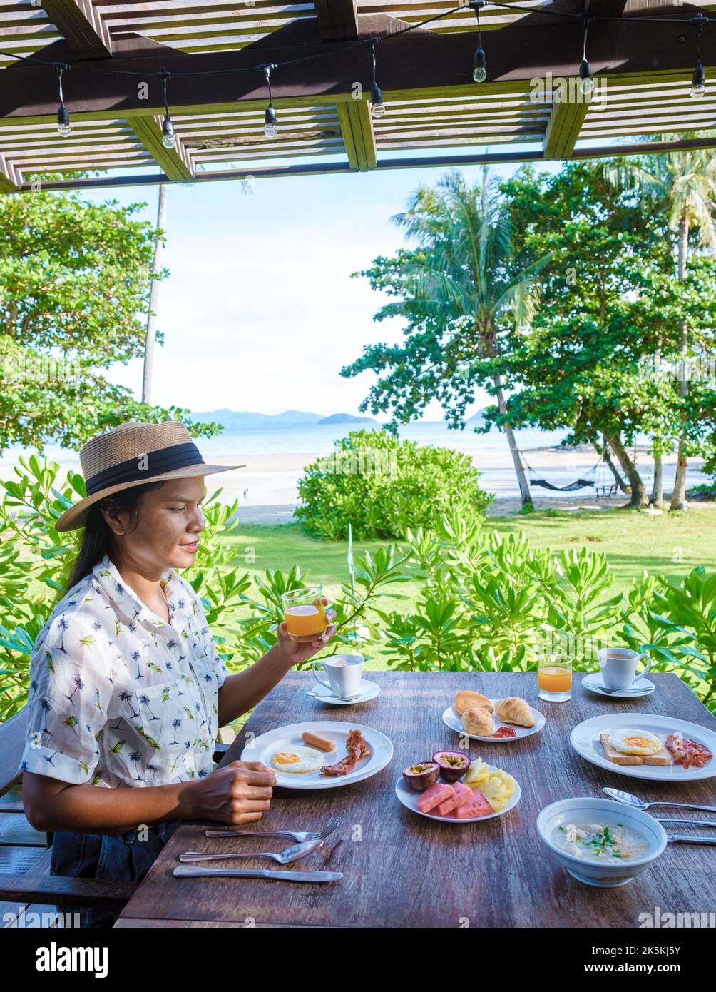 women with a breakfast table on the beach with palm trees in Thailand ...