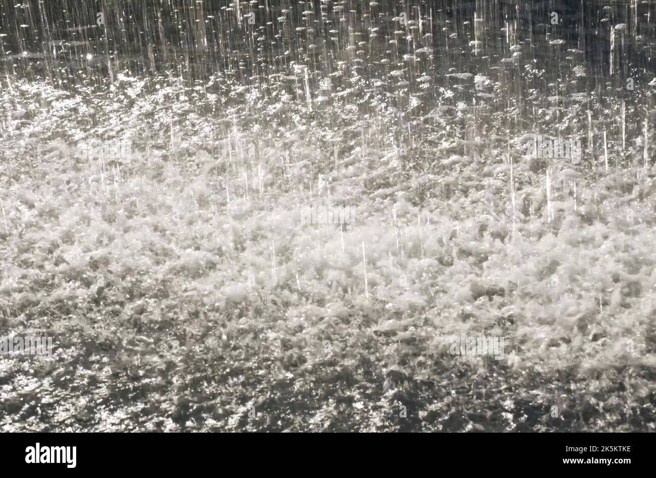 Large drops of rain fall into a puddle of water. Heavy rain, downpour ...