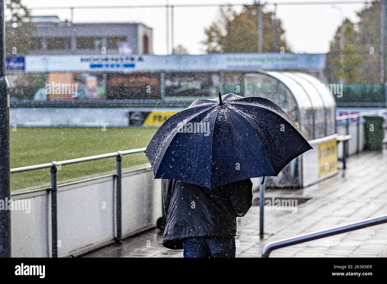 Rear view of a man walking with an umbrella on rainy day next to a ...
