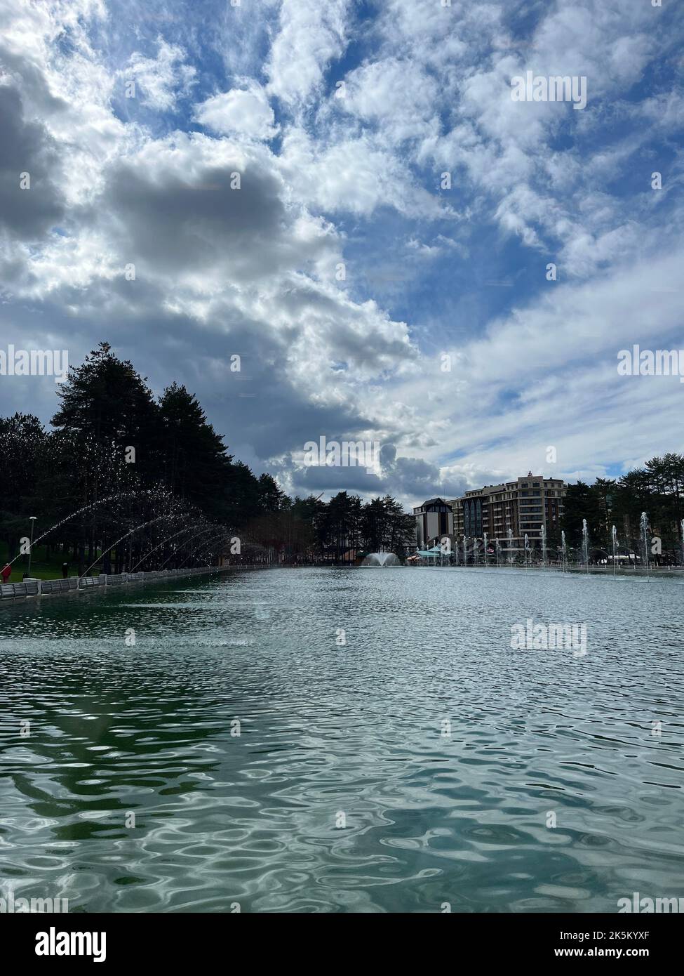 A vertical view of the water fountains in the pond of a city park under ...