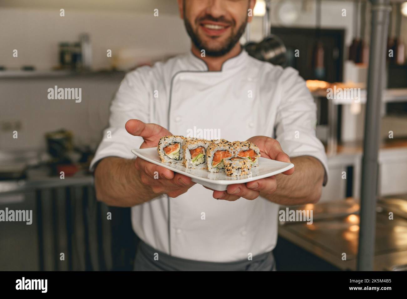 Handsome chef of japanies restaurant showing plate with sushi standing ...