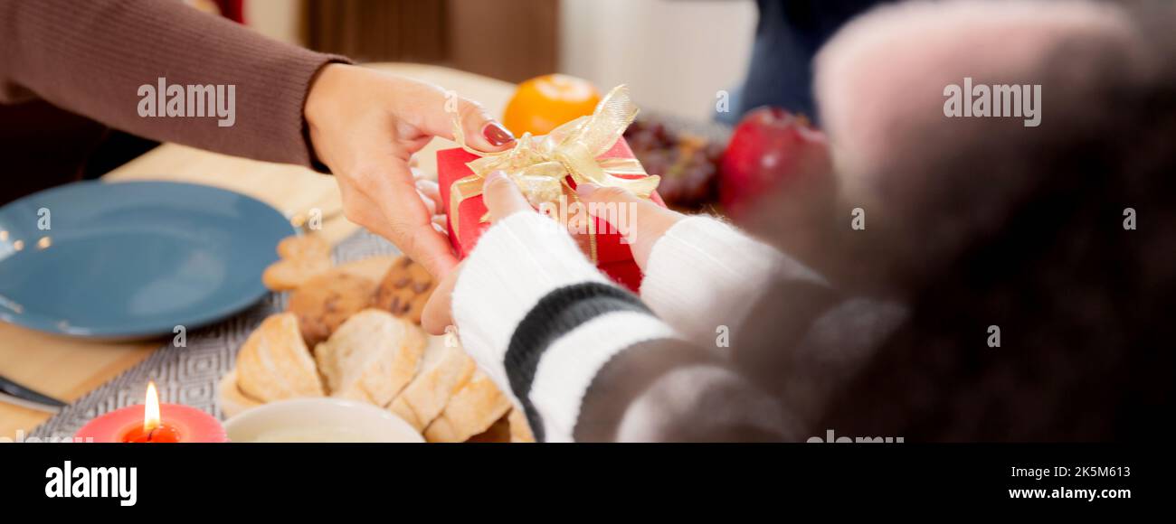 Happy family with daughter giving gift box with mother during dinner at ...