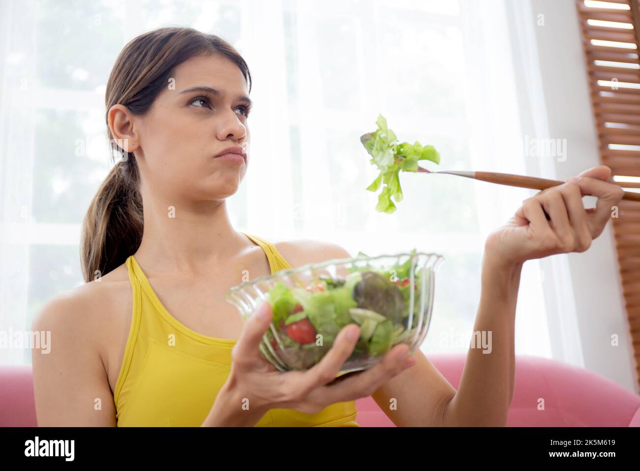 Young caucasian woman sitting on sofa eating vegetable salad while ...