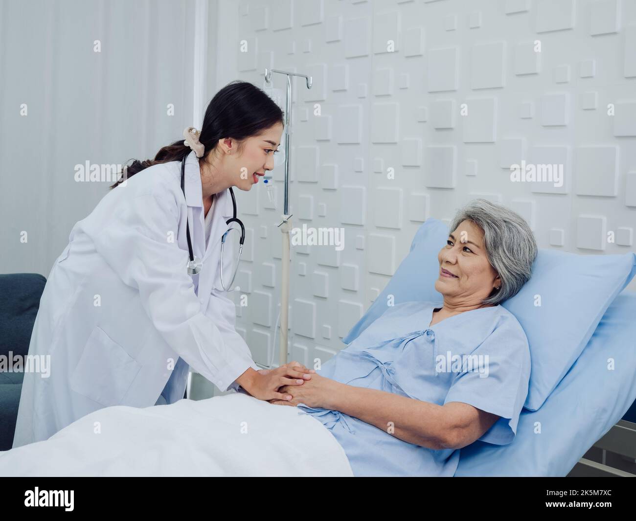 Happy Asian elderly senior woman patient in light blue dress lying on bed in saline solution was ...