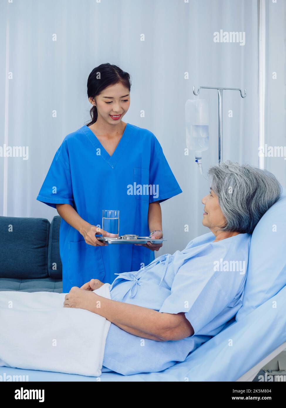 Friendly smiling young Asian nurse in blue scrub holding tray of pills ...