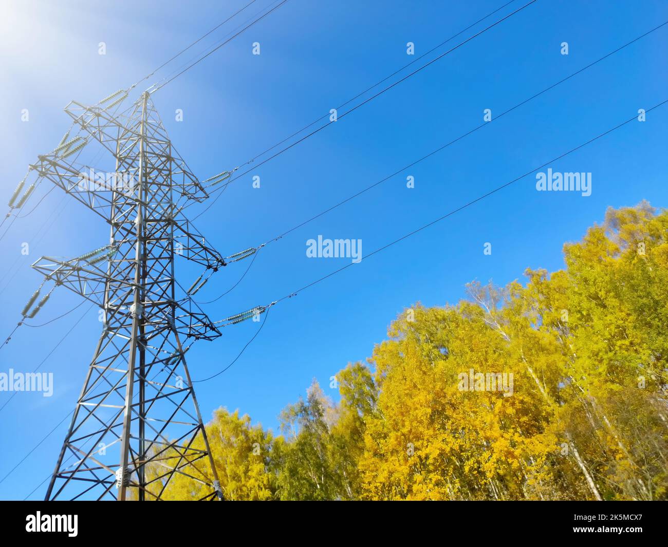Power lines and a tower against a background of blue sky an sun in ...