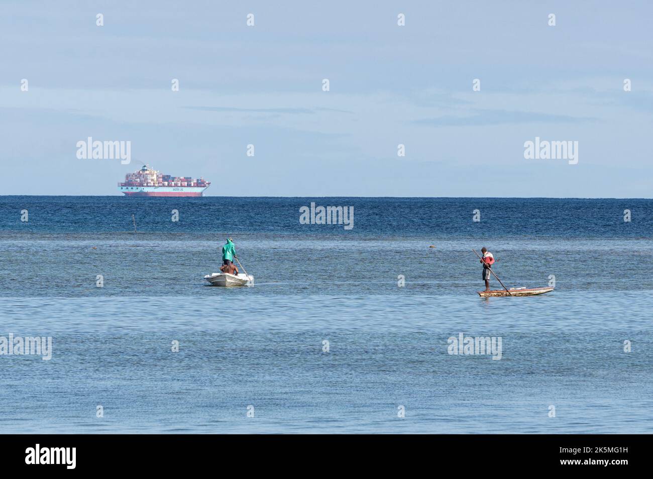 Fishermen in rowing boats with a large shipping tanker on the horizon ...