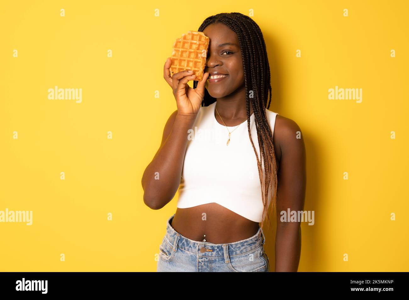 Young beautiful african woman eating sweet waffle pastry over yellow ...