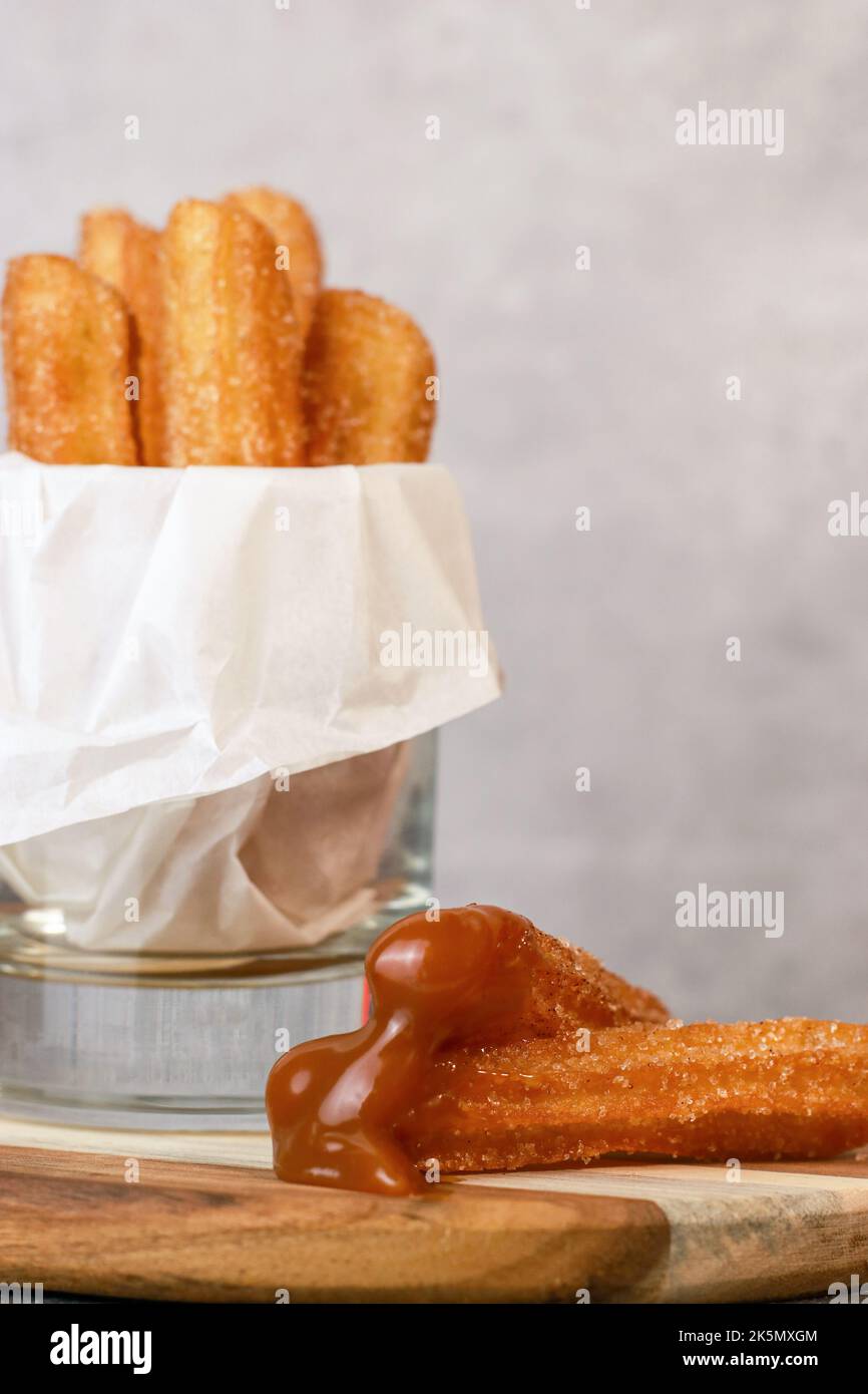 Churros with sugar and caramel sauce in a glass, grey table with copy ...