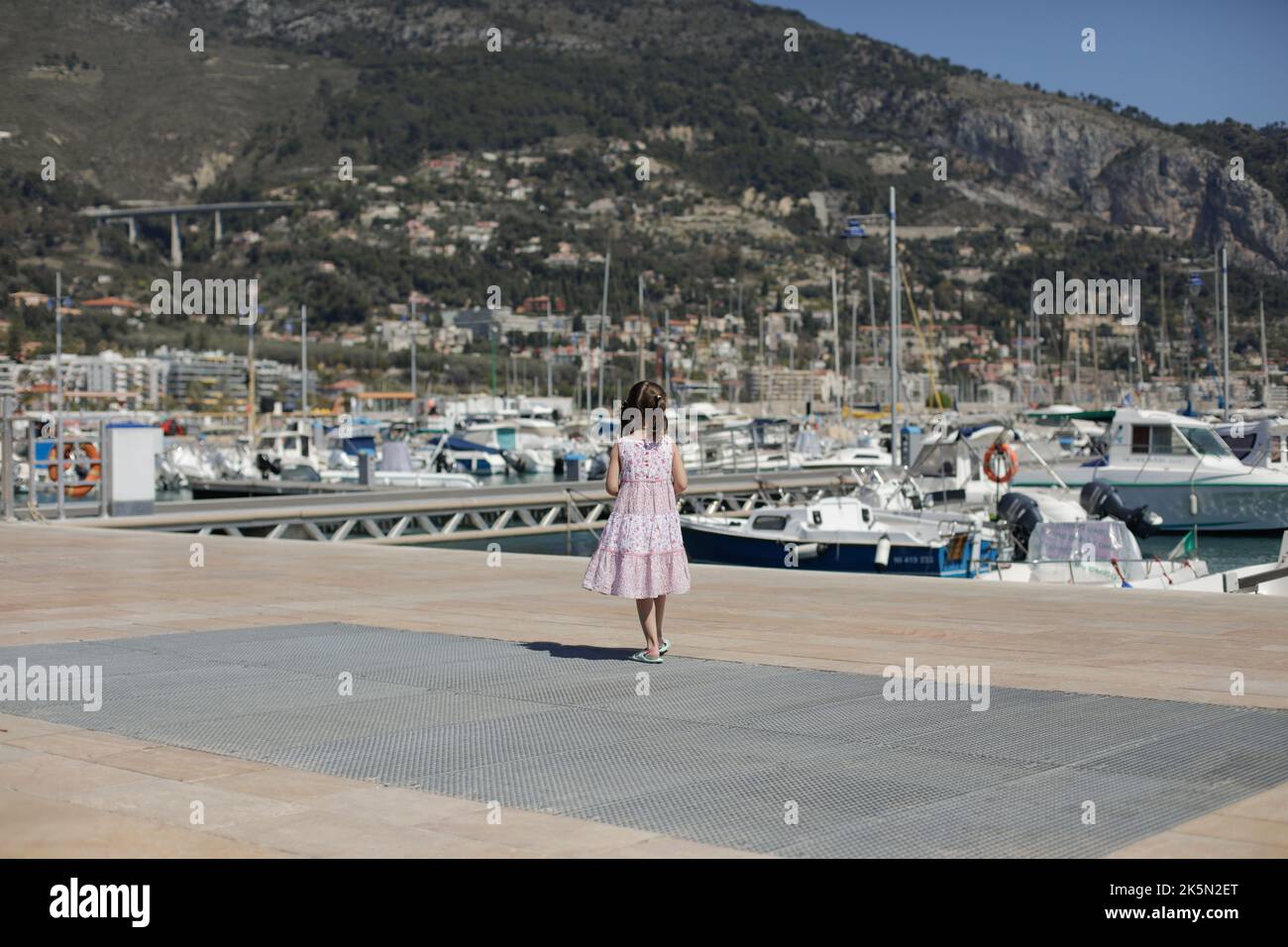 Little girl standing in a marina on the French riviera during a sunny ...