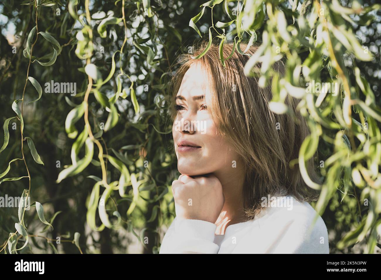 Woman smiling under willow tree in sunlight with shadow from branches ...
