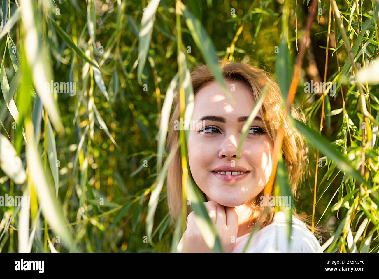 Cute woman smiling under willow tree in sunlight with shadow from ...