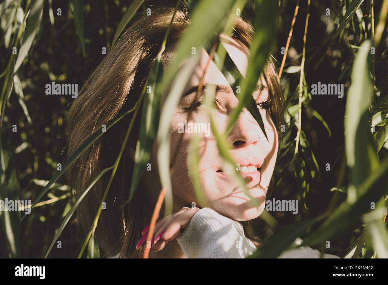 Woman smiling under willow tree in sunlight with shadow from branches ...