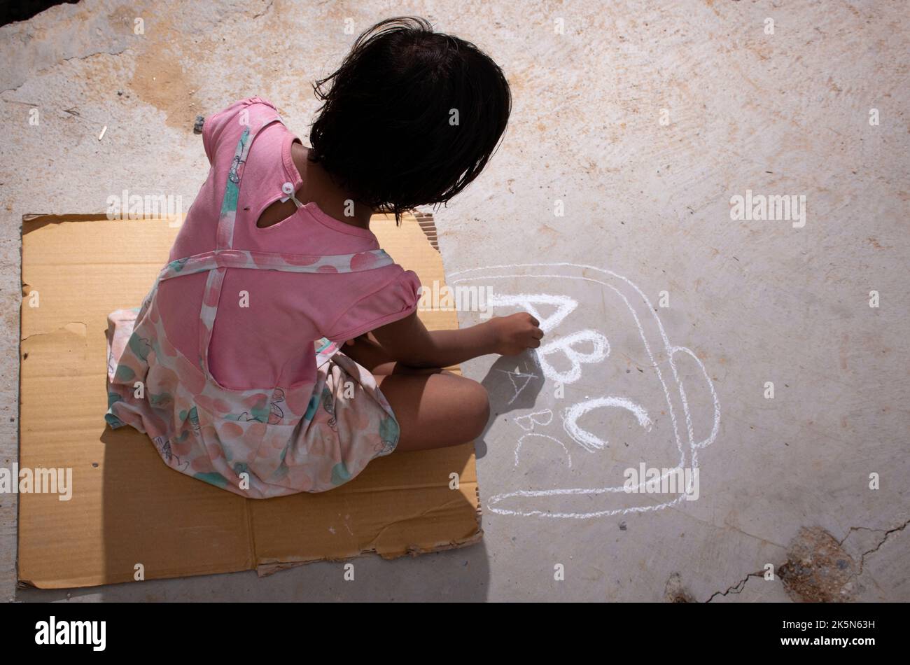 poor child studying and writing on road with chalk in absence of books ...