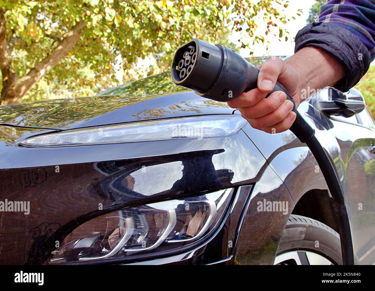Hand holding an electric car charging lead with black electric car ...