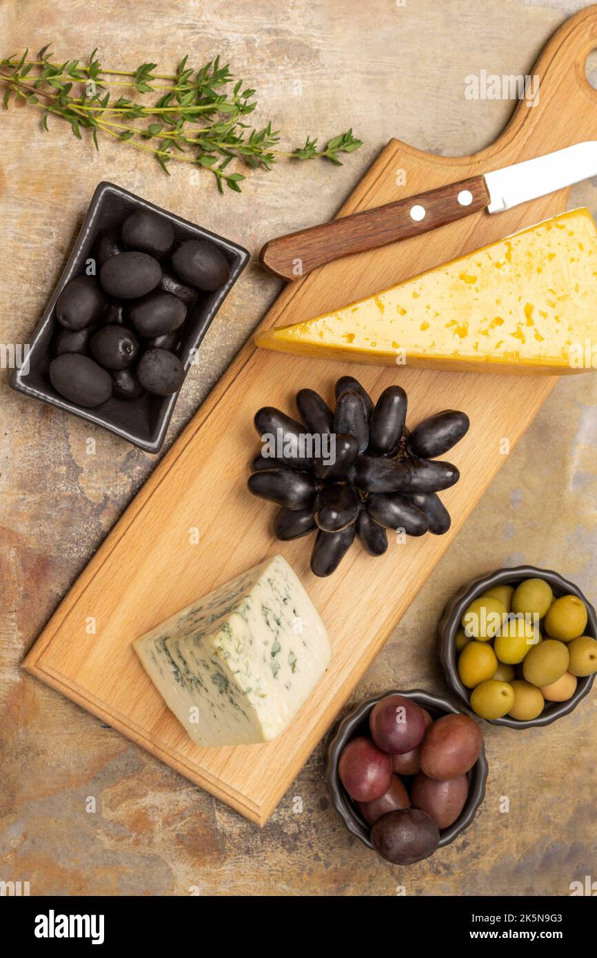 Two pieces of cheese and knife on the board. Green, red and black ...