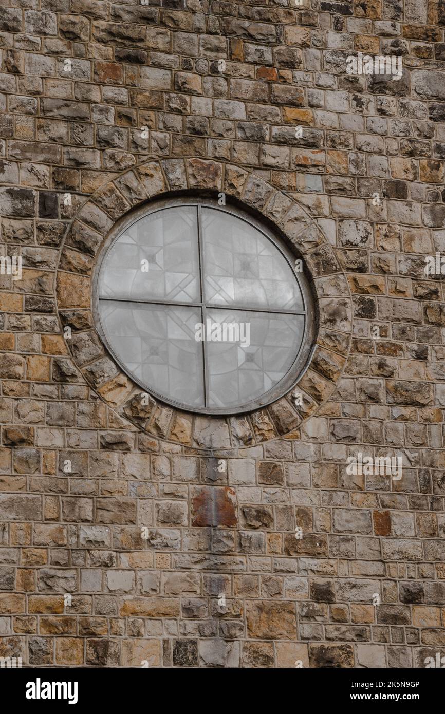A vertical shot of circle glass window in stones wall of old medieval ...