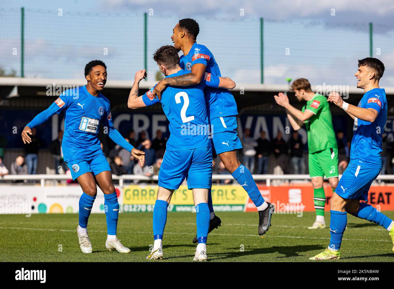 A football team celebrates after scoring a goal while an opposition ...
