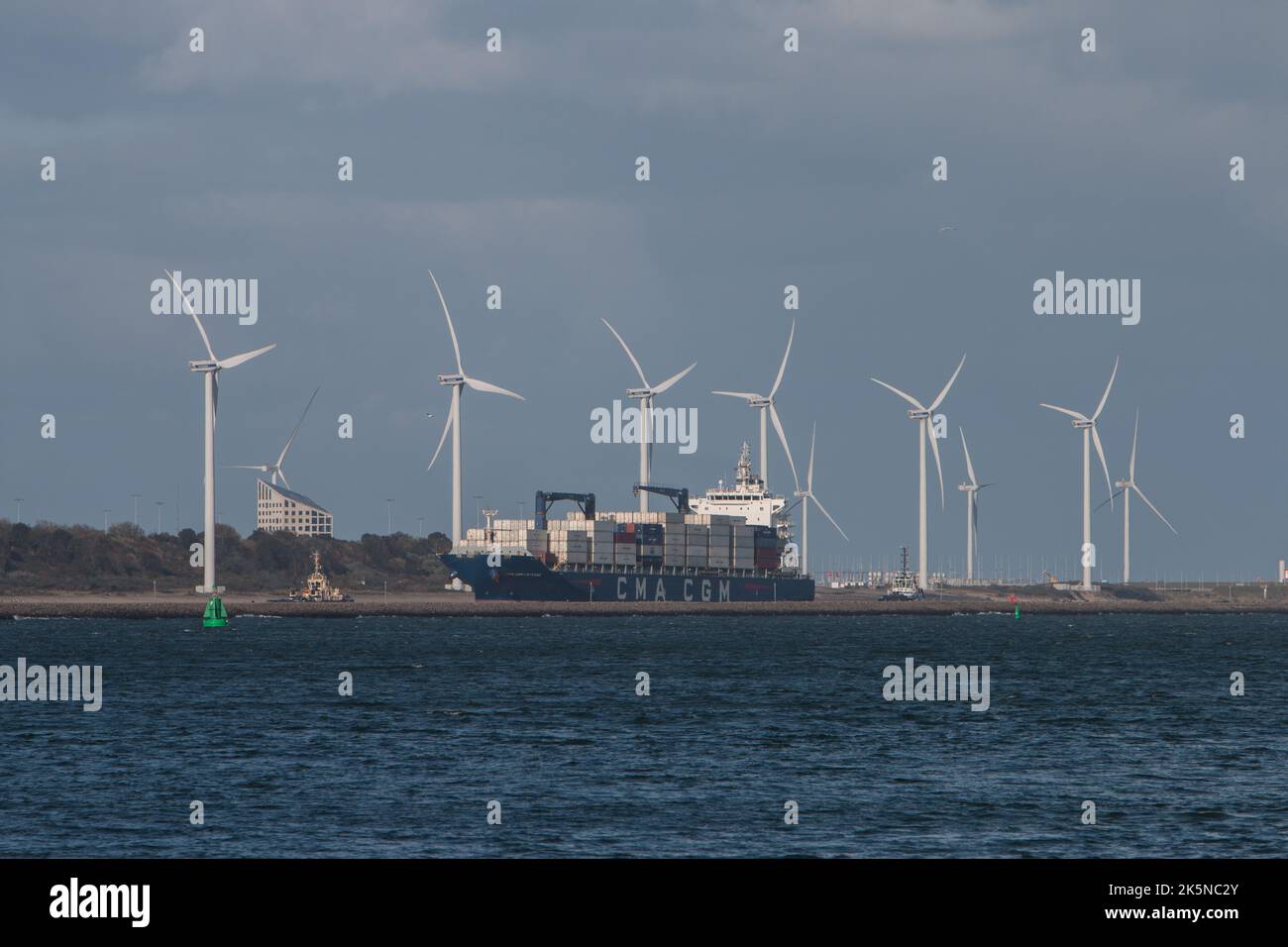 Container ship moving up the waterway passing by onshore wind turbines ...