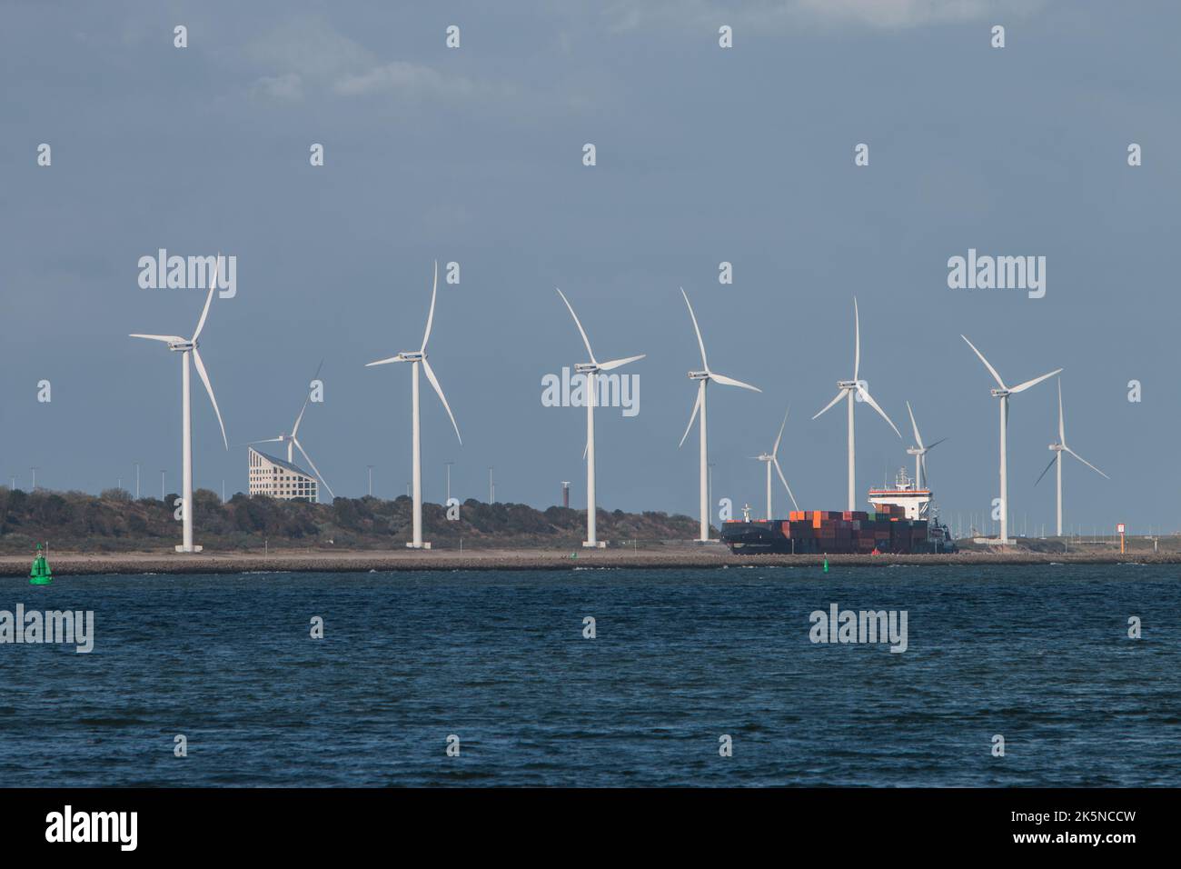 Container ship moving up the waterway passing by onshore wind turbines ...