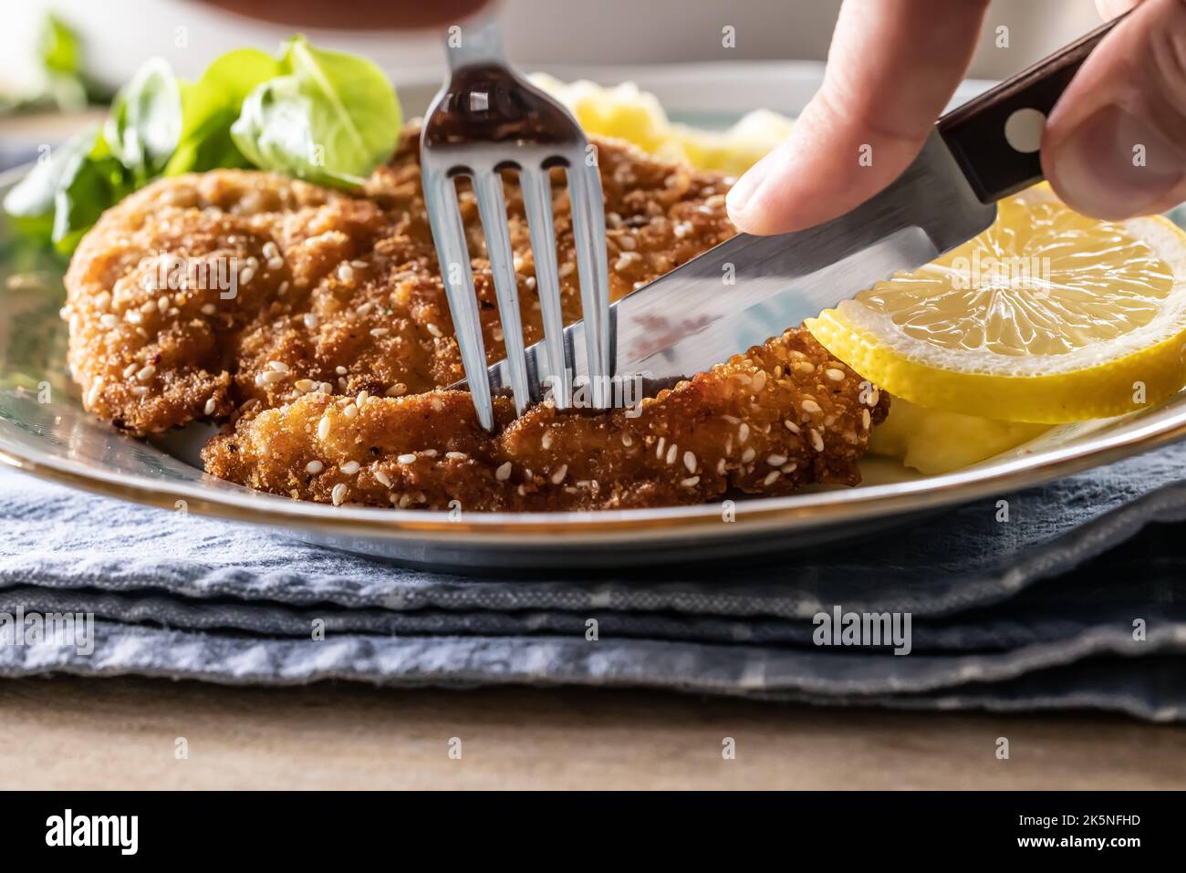 Fork and knife taking a first cut from a schnitzel in sesame seeds ...