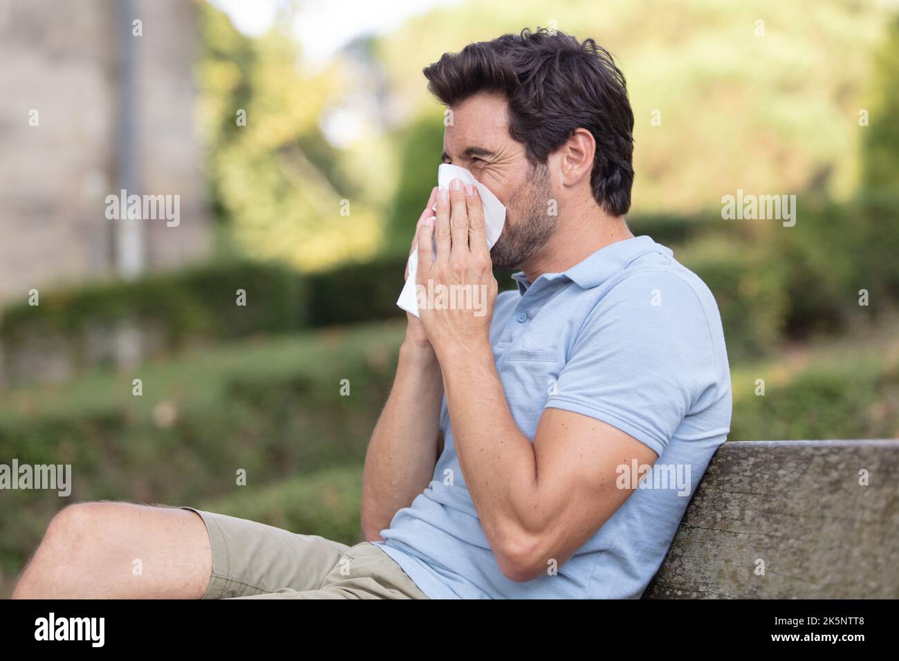 man blowing nose on tissue scene in park Stock Photo - Alamy