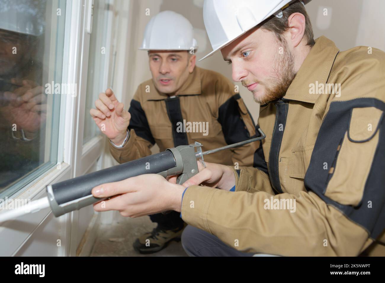apprentice being advised how to apply caulk to window Stock Photo - Alamy