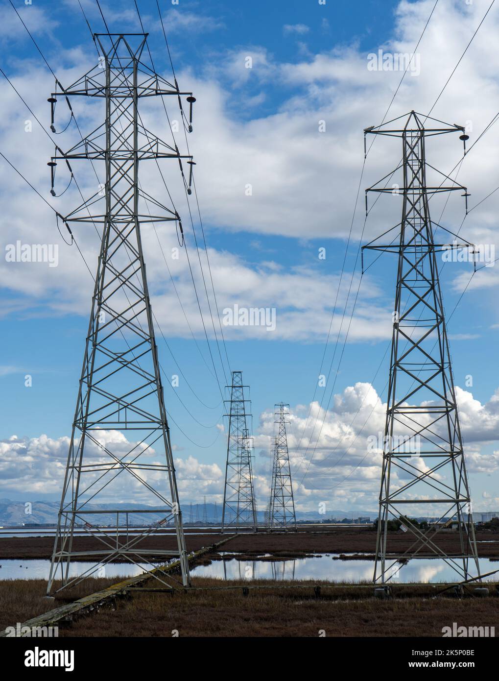 A vertical shot of transmission lines on a grass field on a sunny day ...