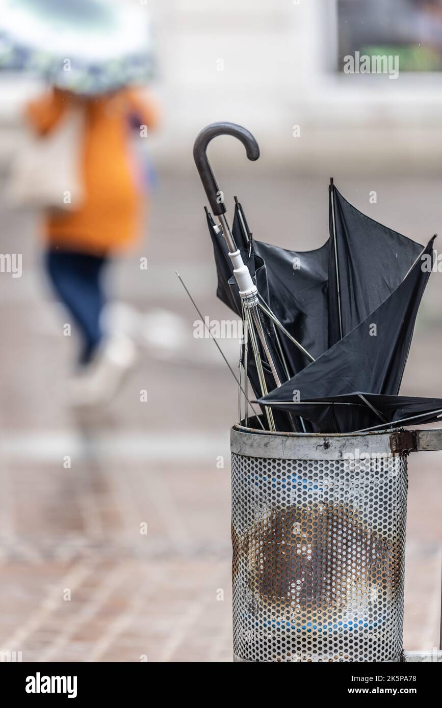 Umbrella damaged by the wind gust is thrown into a street bin on a ...