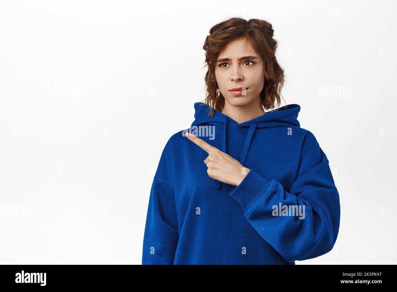 Confused young woman looking and pointing finger at smth strange or bad ...