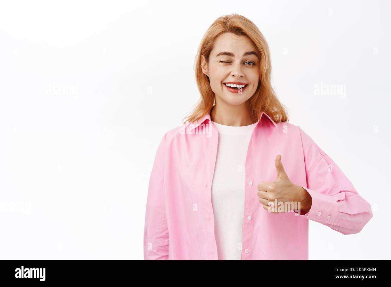 Young woman winks and shows thumb up, approves smth good, praise and ...