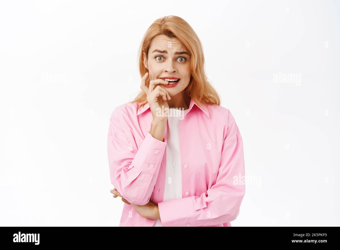Scared and anxious young woman biting finger, looking worried at camera ...