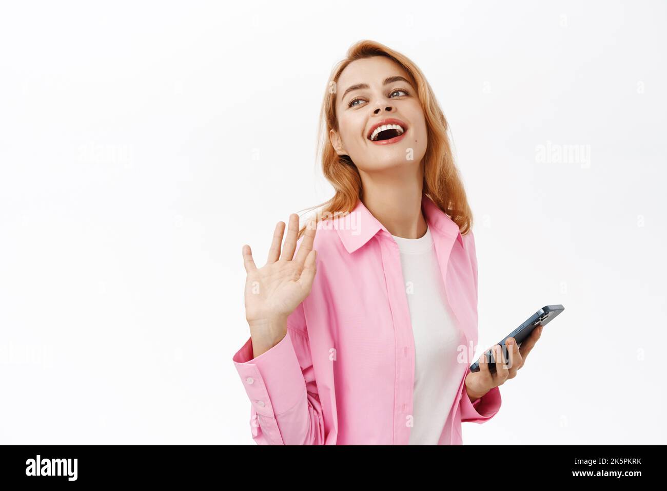 Happy chatting girl holding smartphone and saying hello to someone ...