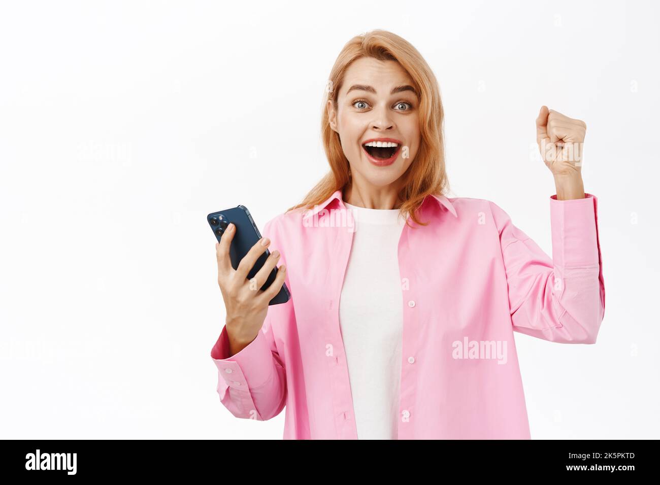 Excited young woman rejoicing, raising hand up and celebrating, holding ...