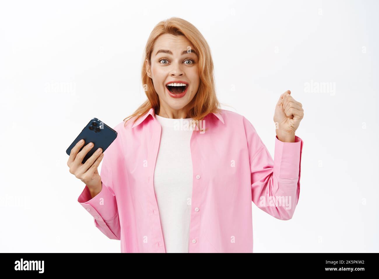 Excited young woman rejoicing, raising hand up and celebrating, holding ...