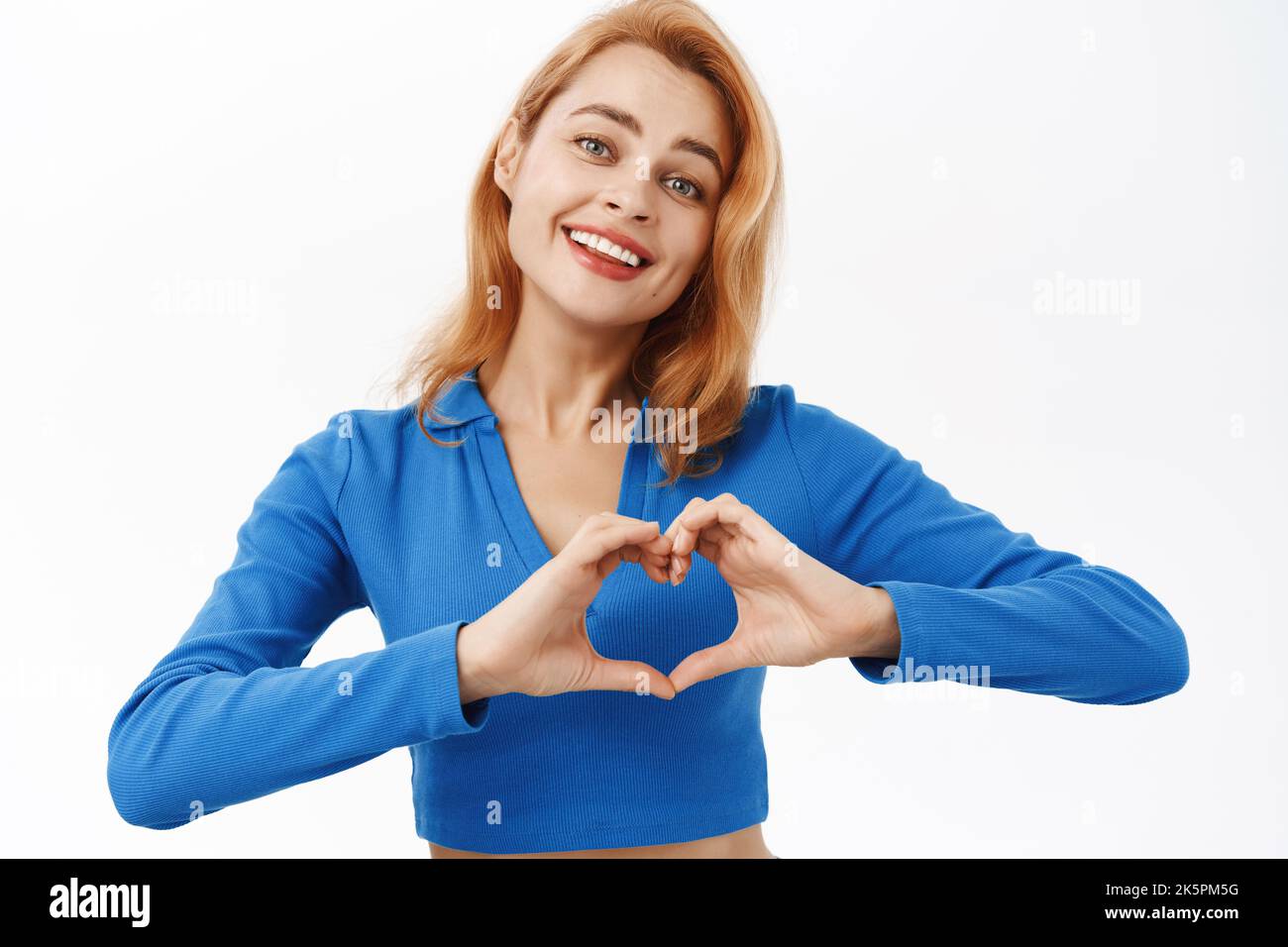 Close up portrait of natural young woman, shows heart sign and looks ...