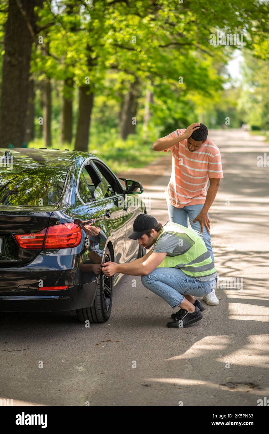 Service man examining the broken wheel of a broken car in the forest ...